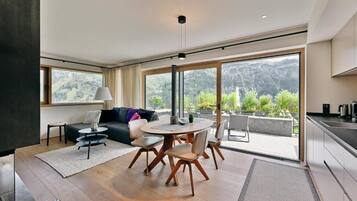 Uma sala de estar moderna com uma mesa de jantar redonda, um sofá e vista para montanhas através de grandes janelas.