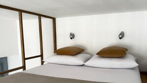 Quarto moderno com cama grande, piso de madeira, paredes brancas e uma janela.