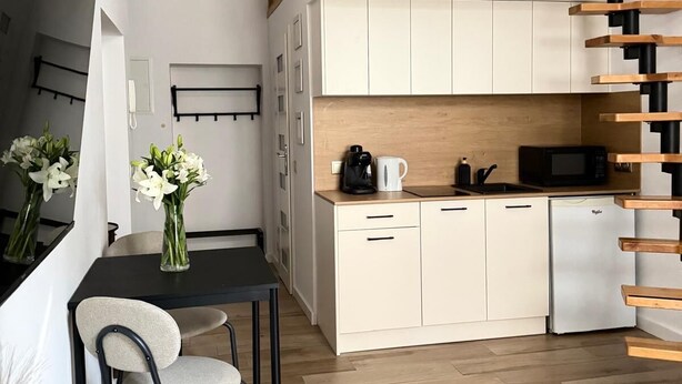 Uma cozinha compacta com área de refeições, uma escada e uma pequena mesa com um vaso de flores.