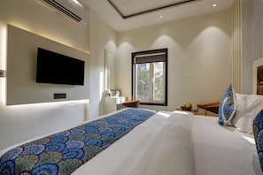 Quarto de hotel com cama, televisão de tela plana na parede, janela com vista e uma pequena mesa com cadeira.