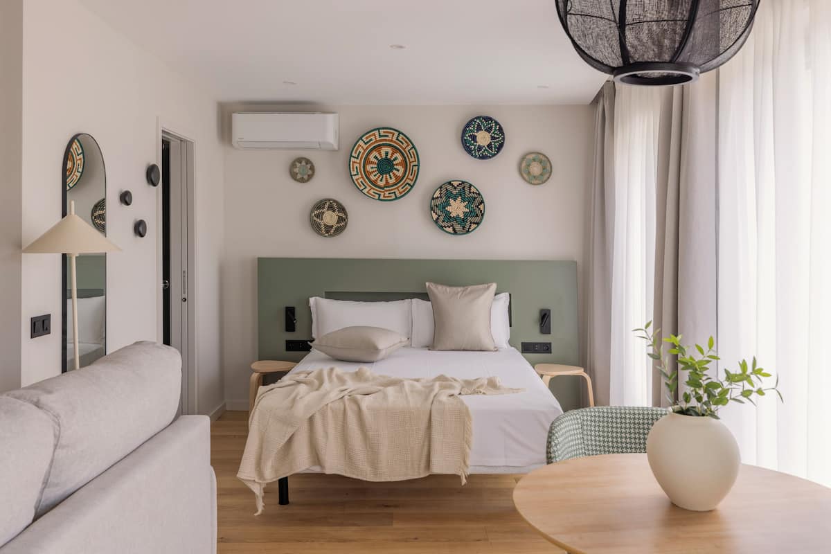 Quarto moderno com cama, mesas de cabeceira, luminária, planta e pratos decorativos na parede.