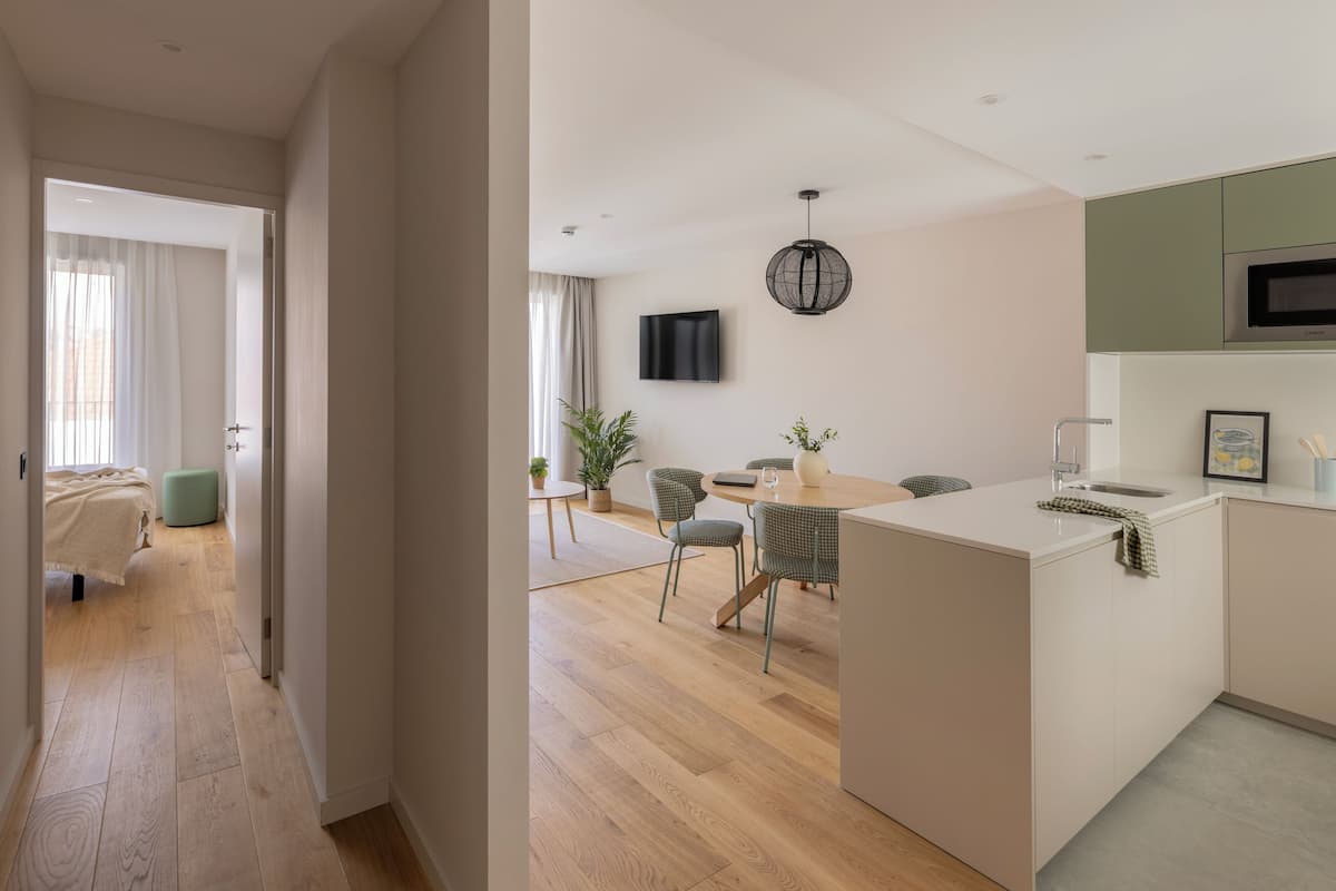 Uma cozinha moderna com uma televisão de tela plana, uma sala de jantar com mesa e cadeiras, e um corredor que leva a um quarto.