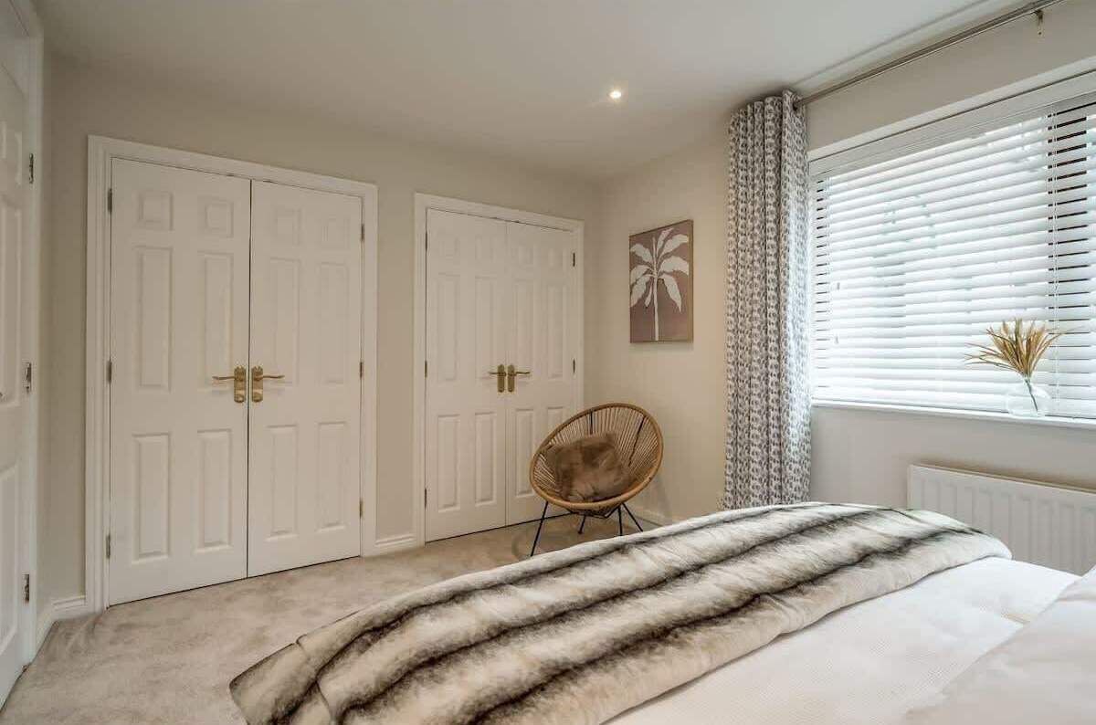 Quarto com uma cama grande, uma cadeira, uma janela com persianas e uma porta com puxador decorativo.