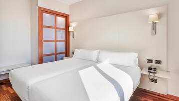 Quarto de hotel com cama grande, porta de madeira, mesa de cabeceira com abajur e telefone fixado na parede.