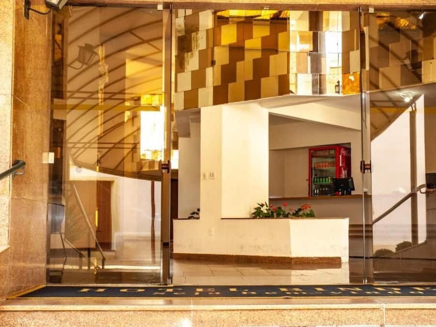 Um saguão de hotel com balcão de recepção, escadaria e refrigerador de Coca-Cola.