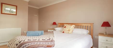 Quarto com cama, mesas de cabeceira, luminária, radiador e um quadro pendurado na parede.