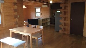 Um interior em madeira com uma mesa de jantar e cadeiras, uma área de cozinha com armários e um frigorífico, e uma porta.