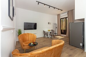 Uma sala de estar moderna com sofá, área de jantar com mesa e cadeiras, televisão de tela plana na parede e geladeira.