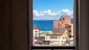 Vista costeira através de uma janela, mostrando edifícios, céu claro e o mar.
