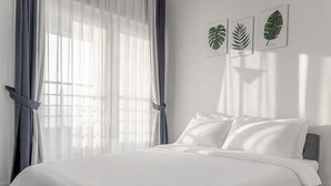 Um quarto com cama, cortinas brancas e três quadros com impressões de folhas na parede.