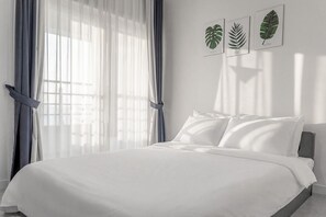Um quarto com cama, cortinas brancas e três quadros com impressões de folhas na parede.