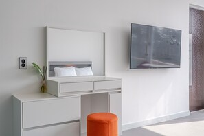 Quarto moderno com um espelho grande, uma mesa de cabeceira, uma cadeira e uma TV fixada na parede.