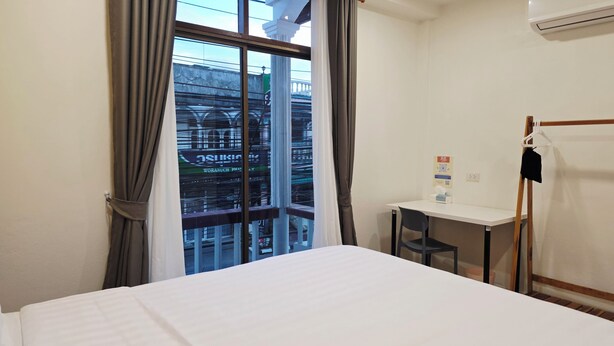 Quarto de hotel com cama, escrivaninha, cadeira, janela com cortinas e vista para a paisagem urbana.