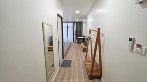 Um corredor com piso de madeira, um espelho, um escorredor de sapatos de madeira, uma mesa com cadeira e um telefone fixado na parede.