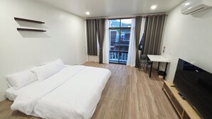 Quarto de hotel com cama, televisão, escrivaninha e varanda com cortinas.