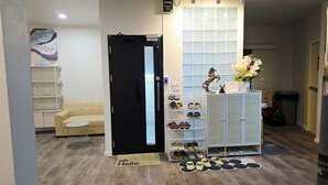 Uma área de recepção com uma porta preta, um sofá, uma vitrine de sapatos e um calendário na parede.