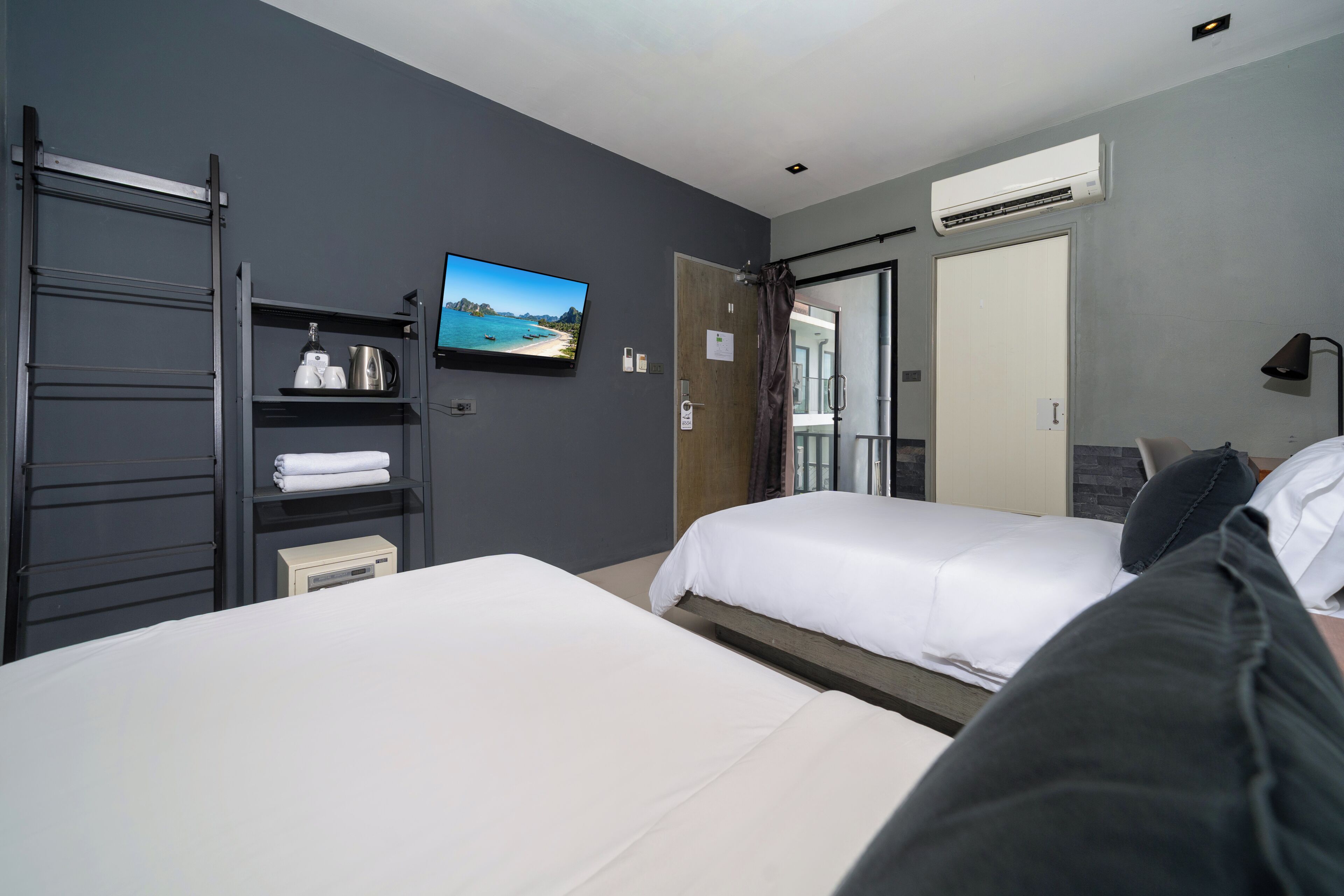 Quarto de hotel com duas camas, televisão, prateleira com amenities e ar condicionado.