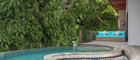 Piscina com hidromassagem, cercada por vegetação exuberante e um deck de madeira.