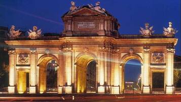 Um arco imponente e iluminado, com esculturas clássicas e inscrições, provavelmente um monumento histórico.