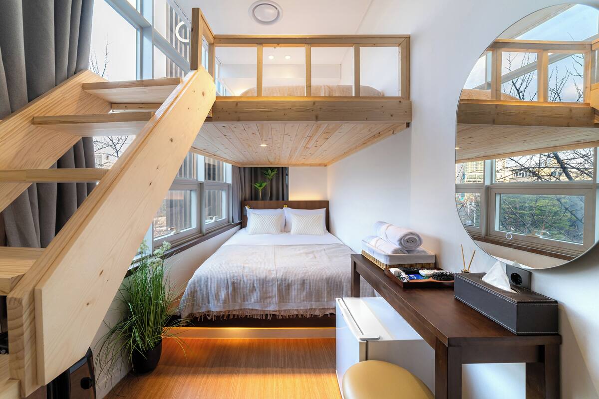 Quarto com cama beliche, escrivaninha, cadeira, espelho e janela.