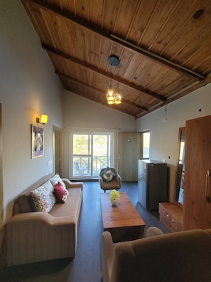 Uma sala de estar aconchegante com teto de madeira, um sofá, uma mesa com um vaso e vista através de uma porta de vidro.
