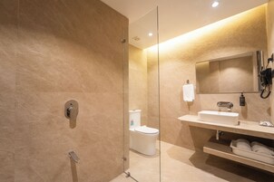 Uma casa de banho moderna com cabine de chuveiro em vidro, sanita branca, lavatório com espelho e um porta-toalhas.