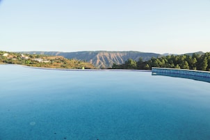 Piscina transparente com vista para colinas distantes e alguns edifícios.