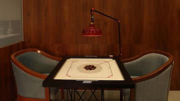 Quarto com paredes de madeira, uma mesa com abajur vermelho e duas cadeiras com estofamento azul claro.