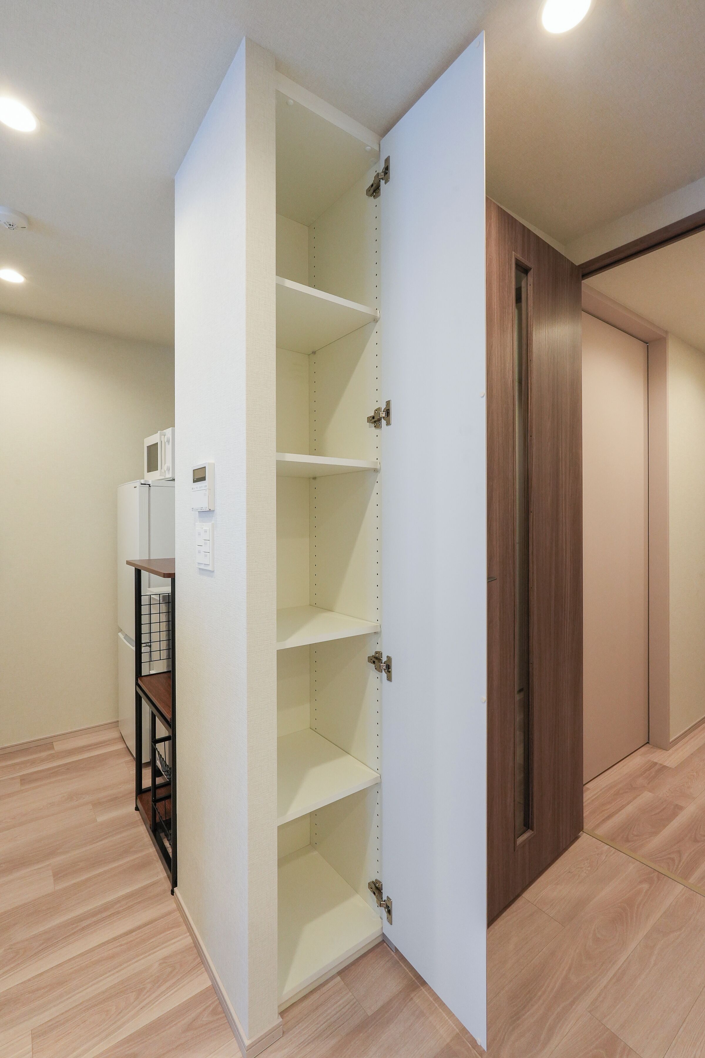 Quarto com guarda-roupa branco, porta de madeira e cozinha equipada com micro-ondas e frigorífico.