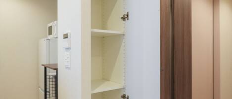 Quarto com guarda-roupa branco, porta de madeira e cozinha equipada com micro-ondas e frigorífico.