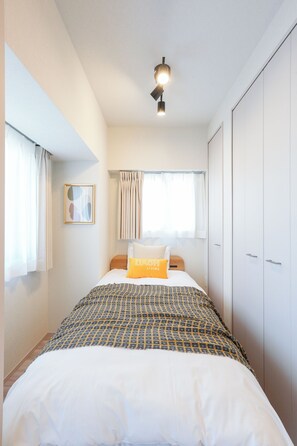Um quarto com cama, mesa de cabeceira, janela com cortinas, luminária na parede e guarda-roupa.