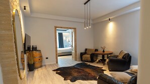 Uma sala de estar moderna com um sofá de couro, uma mesa redonda de madeira e um tapete de pele grande. Há um barril de madeira e um espelho à esquerda.
