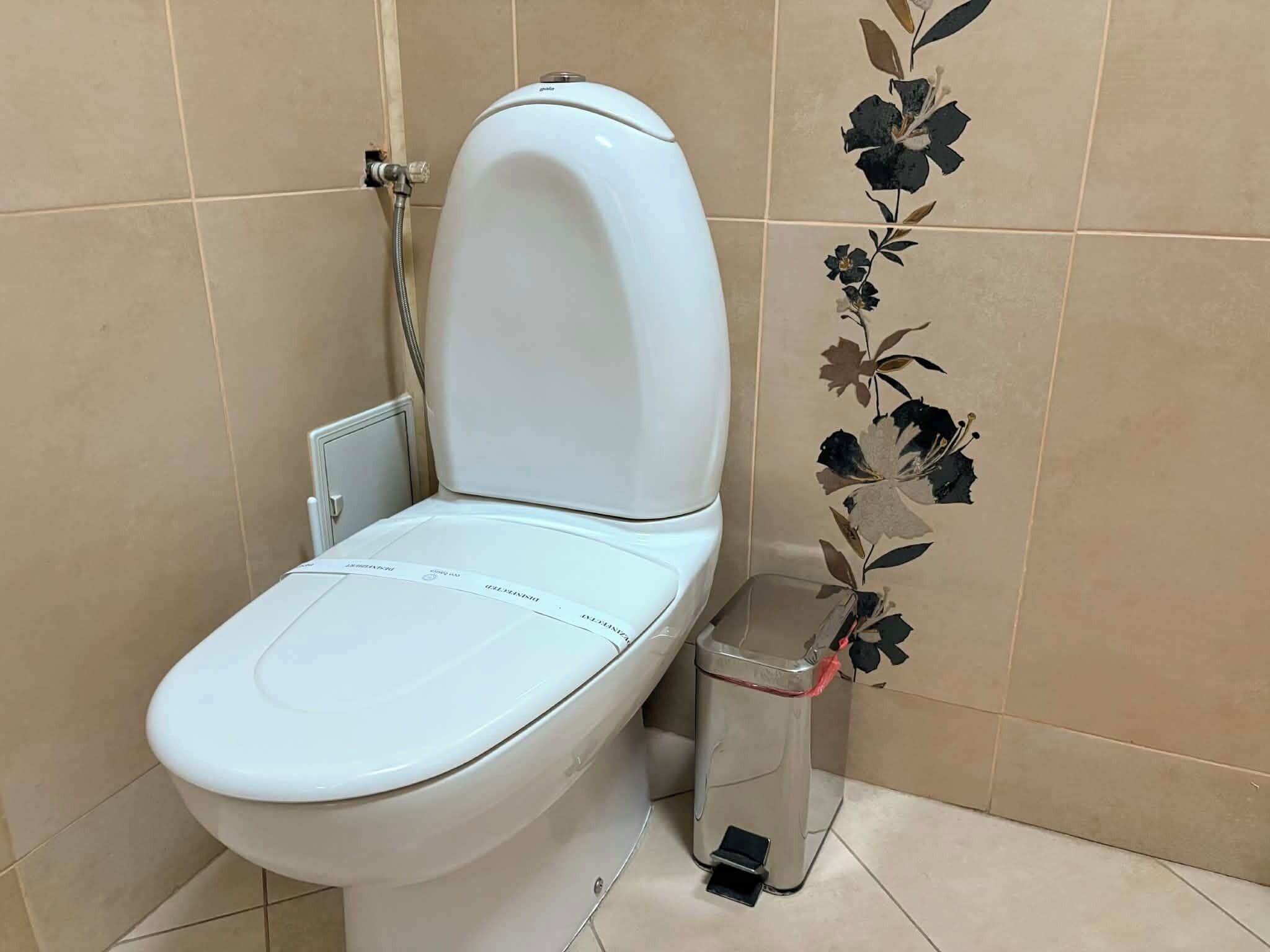 Sanitário com bidê, lixeira e um ornamento floral na parede.