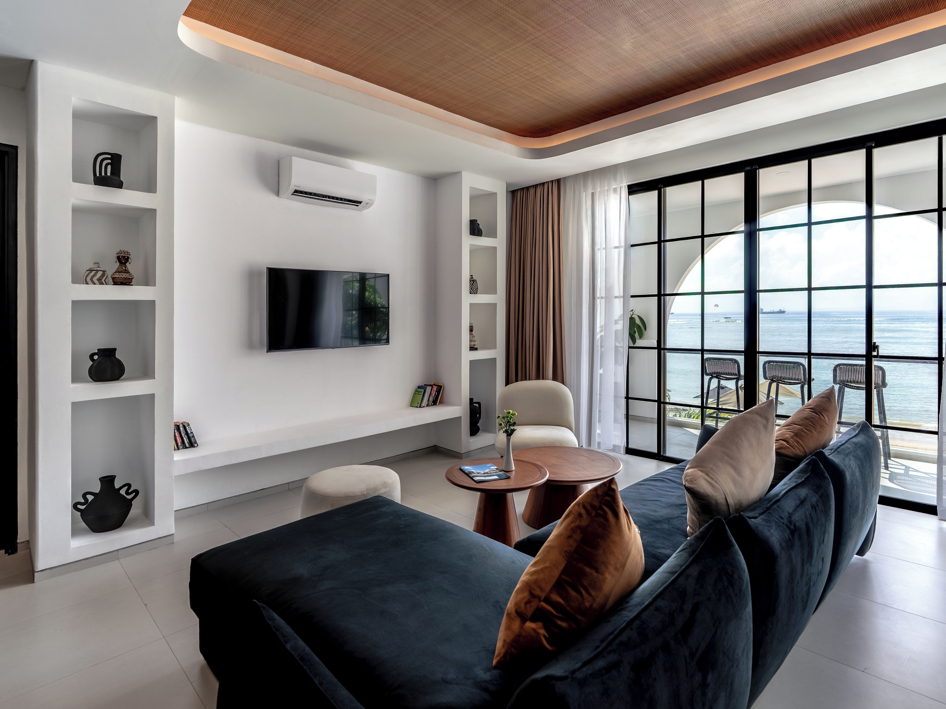Sala de estar moderna com sofá, televisão de tela plana e vista para o mar.