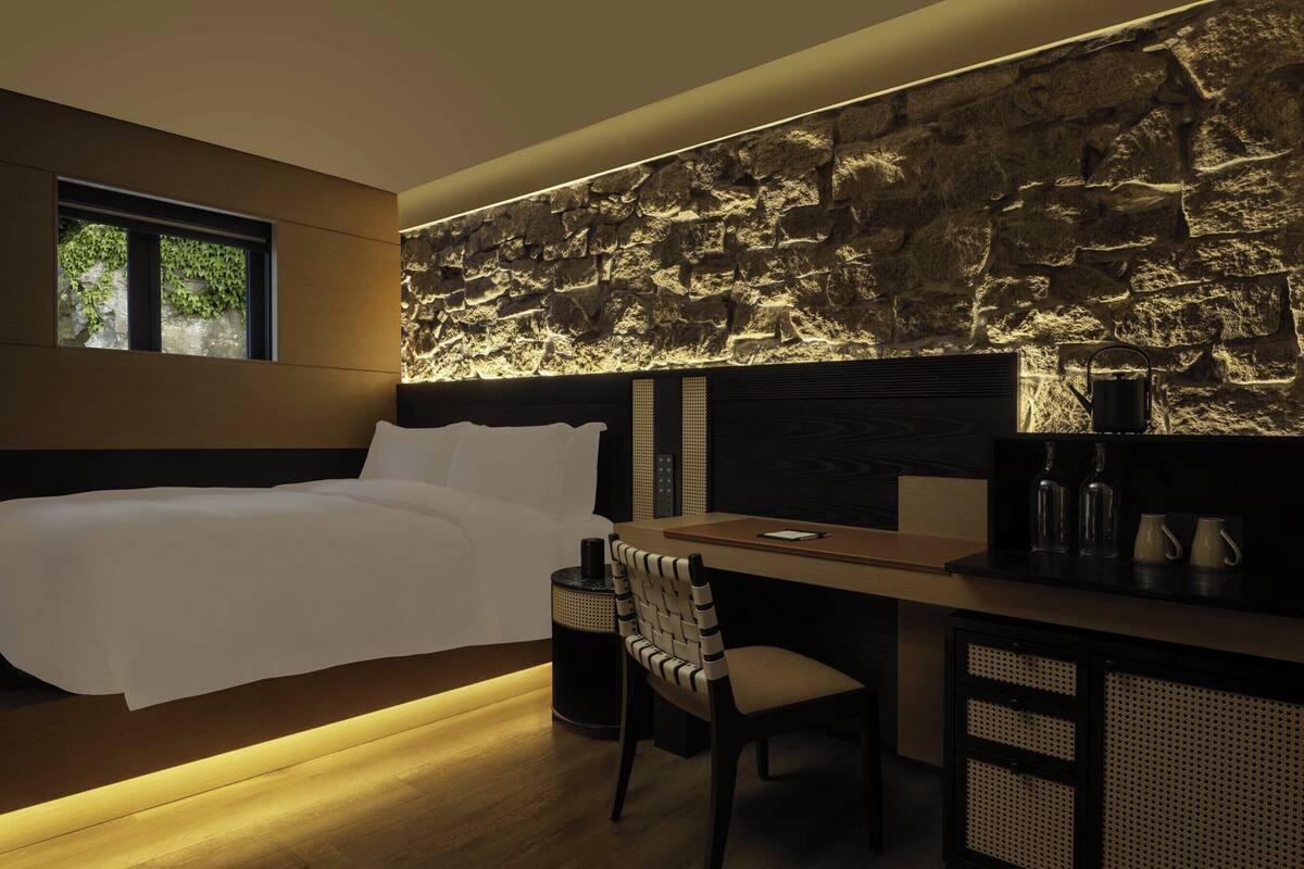 Um quarto com cama, escrivaninha, cadeira e parede de pedra.