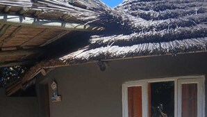 Uma casa com telhado de palha, uma janela com persianas de madeira e chão de concreto.