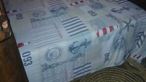 Uma cama com colcha estampada, cabeceira de madeira e cadeira de vime.