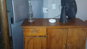 Um armário de madeira com uma garrafa de vidro, um ventilador e um pequeno recipiente branco em cima.