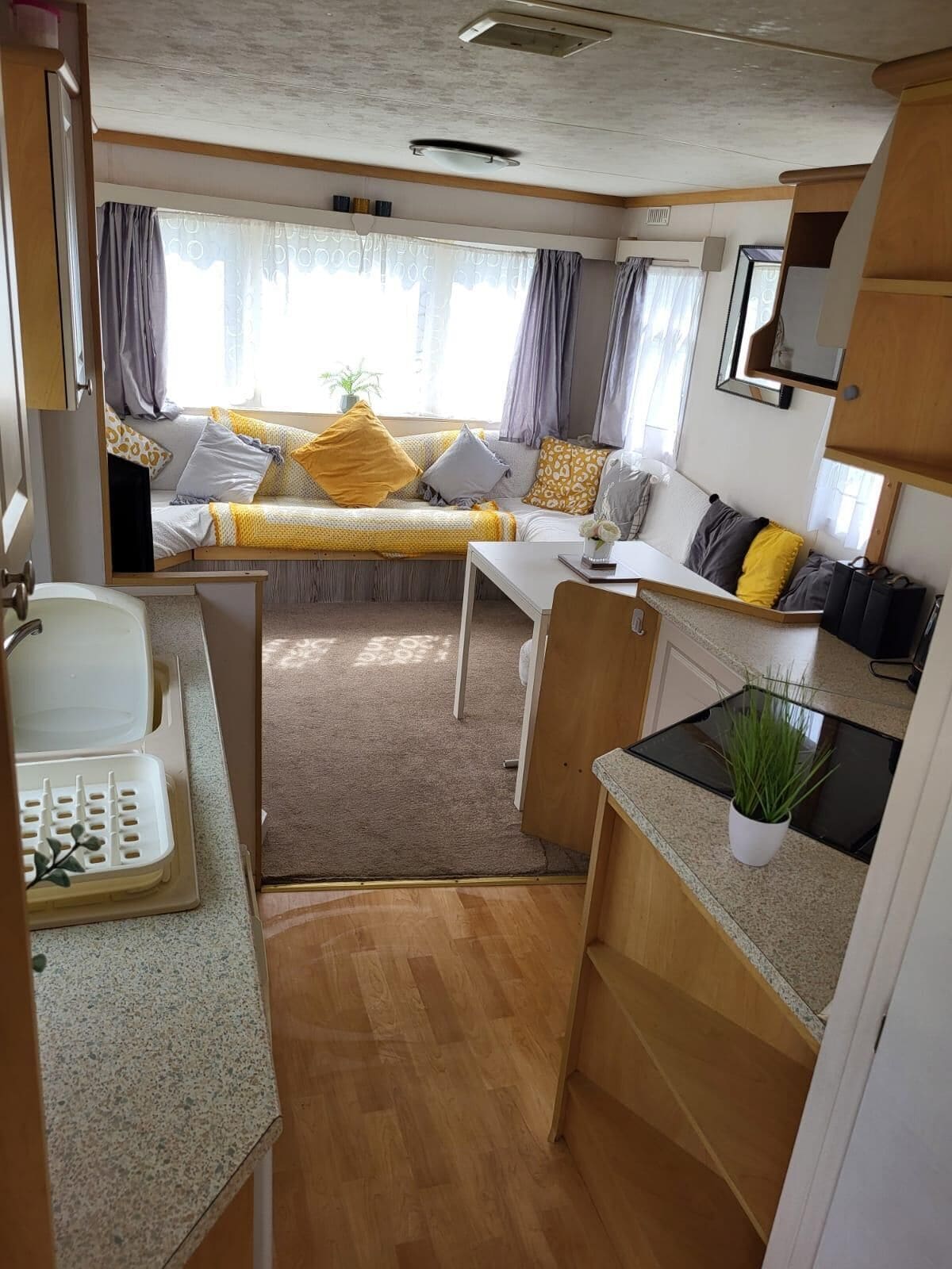 Interior compacto de uma motorhome, com cozinha compacta, área de estar com almofadas e uma pequena mesa.