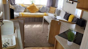 Interior compacto de uma motorhome, com cozinha compacta, área de estar com almofadas e uma pequena mesa.