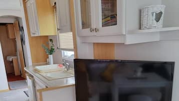 Uma cozinha compacta com armários brancos, uma TV integrada e uma geladeira pequena.