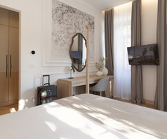 Quarto de hotel com cama, escrivaninha, cadeira, guarda-roupa, espelho, televisão e janela com cortinas.