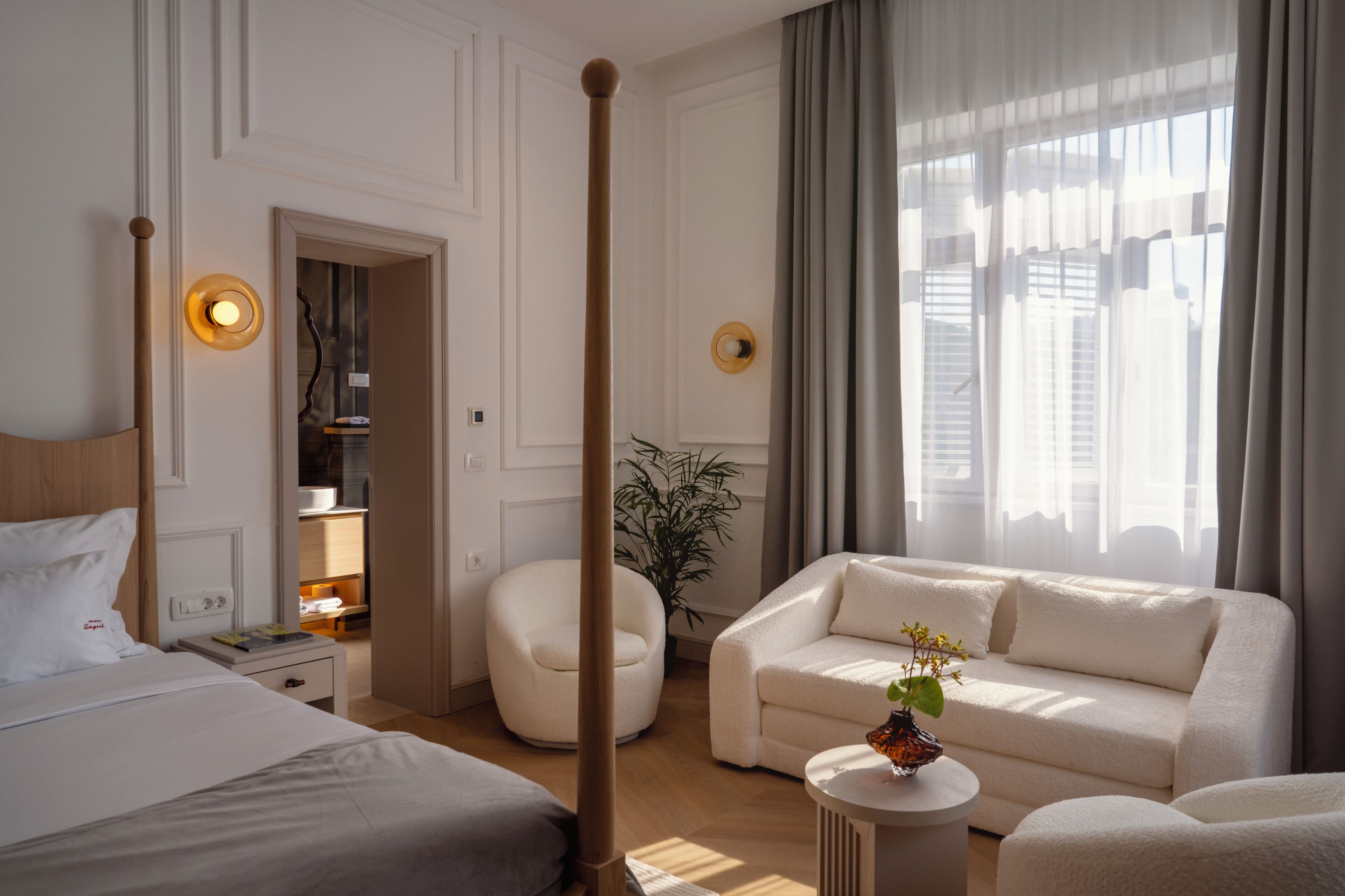 Quarto de hotel com uma cama, um sofá, uma mesinha com um vaso e uma planta.
