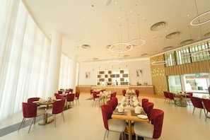 Uma sala de jantar moderna com cadeiras vermelhas, uma mesa comprida posta para refeição e uma luminária contemporânea.