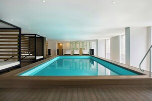 Piscina interior moderna com deck de madeira, escada com guarda-corpo preto e vista do espaço interno.