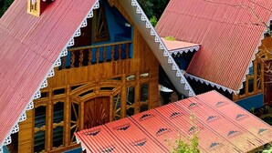 Uma casa de madeira tradicional com telhado vermelho, rodeada por vegetação exuberante e montanhas.