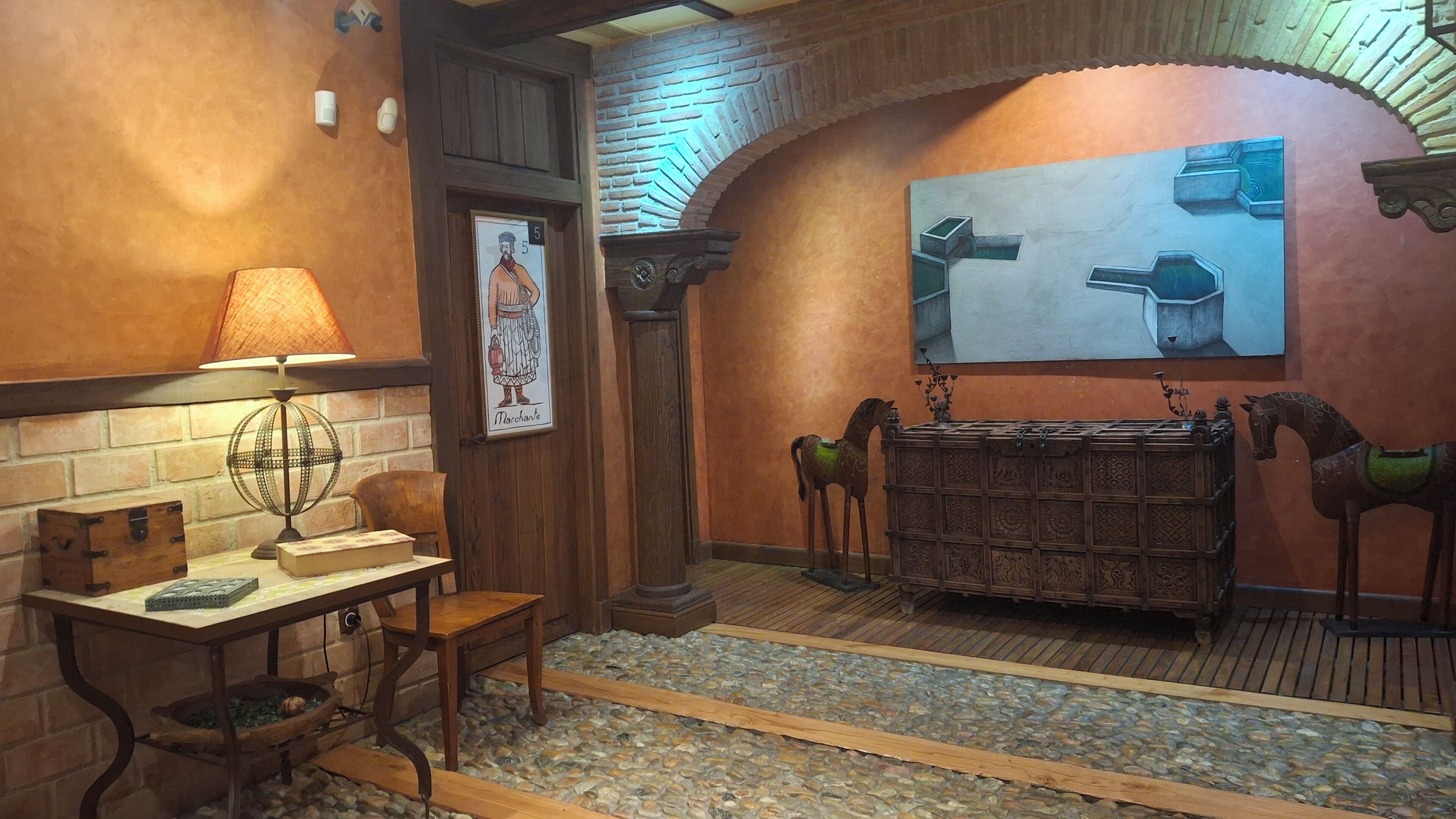 Quarto com uma mesa de madeira, cadeiras, luminária globo, quadro emoldurado, baú e um cavalo decorativo.