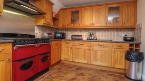 Uma cozinha com armários de madeira, um forno vermelho, micro-ondas e lixeira.