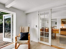 Quarto com cadeira de madeira, porta de vidro que dá para uma sala de jantar e vista para o exterior.