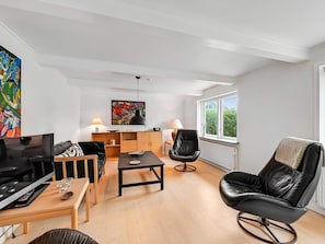 Uma sala de estar moderna com televisão de tela plana, poltronas de couro, mesa de centro de madeira e obras de arte nas paredes.
